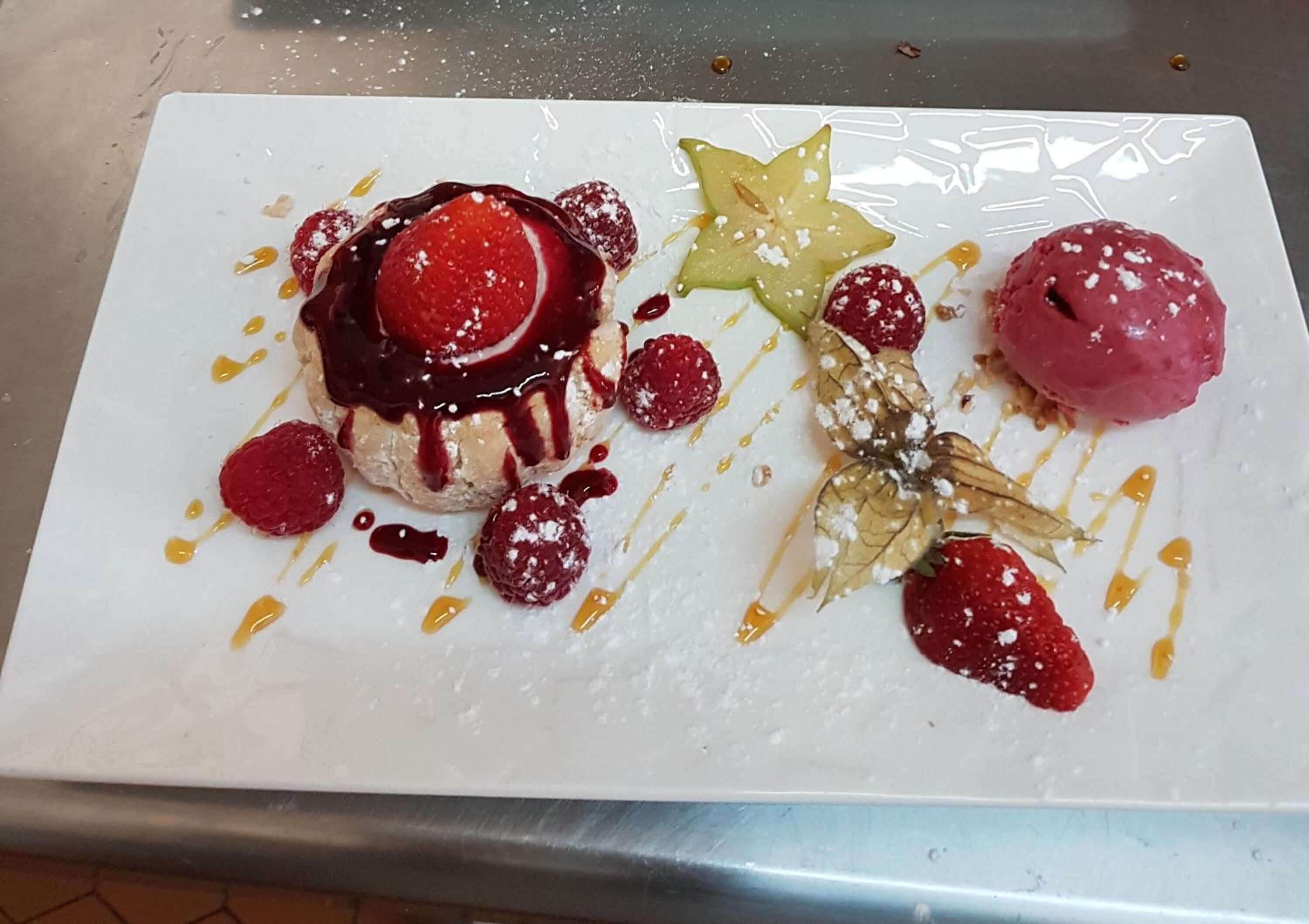 Um prato de sobremesa com uma bola de sorvete, um pastel em formato de estrela e framboesas.