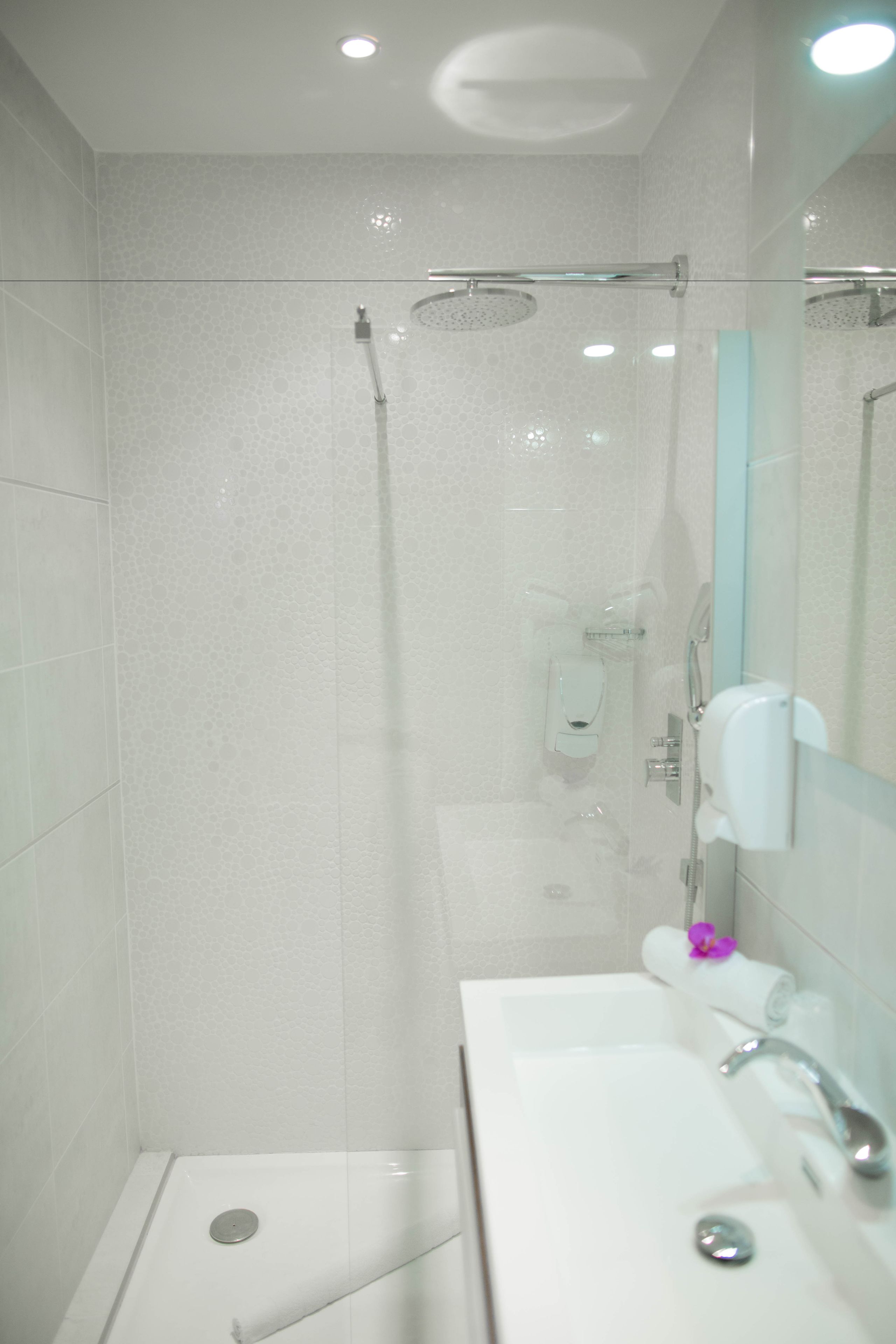Casa de banho moderna com chuveiro envolto em vidro, lavatório branco e chuveiro manual.