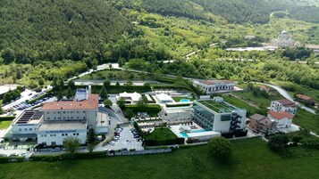 Vista aérea de um complexo hoteleiro com vários edifícios, uma piscina e uma paisagem verde exuberante.