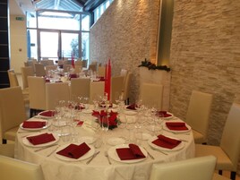 Uma sala de jantar com mesas redondas preparadas para uma refeição, com toalhas brancas e guardanapos vermelhos.