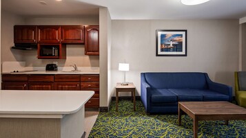 Quarto de hotel compacto com cozinha compacta, um sofá azul, uma mesinha e um tapete estampado.