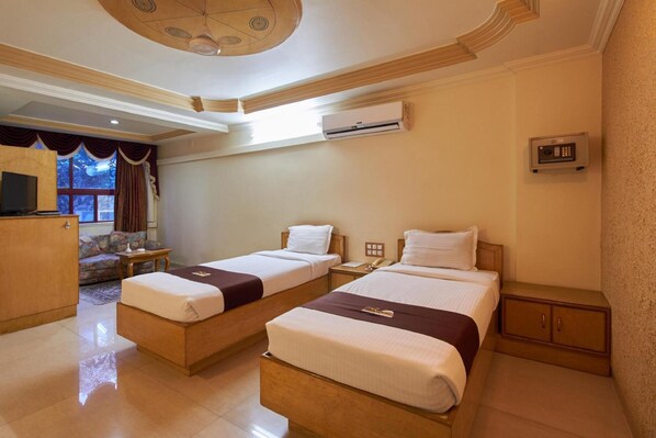 Quarto de hotel com duas camas de solteiro, TV, ar condicionado, escrivaninha e sofá.