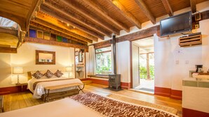 Um quarto espaçoso com uma cama grande, vigas de madeira no teto, televisão e uma janela com vista para o verde.
