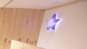 Uma cama beliche de madeira com colchão acolchoado, um luminária em formato de estrela na parede e um batente de porta visível.