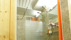 Um chuveiro com box de vidro, chuveiro manual e torneira embutida na parede.