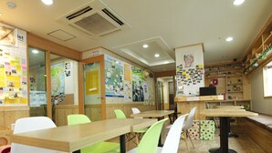Restaurante com mesas e cadeiras de madeira, um mural com fotografias e um balcão com menu.