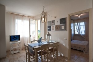 Uma sala de jantar com mesa, cadeiras, televisão e um candeeiro decorativo.