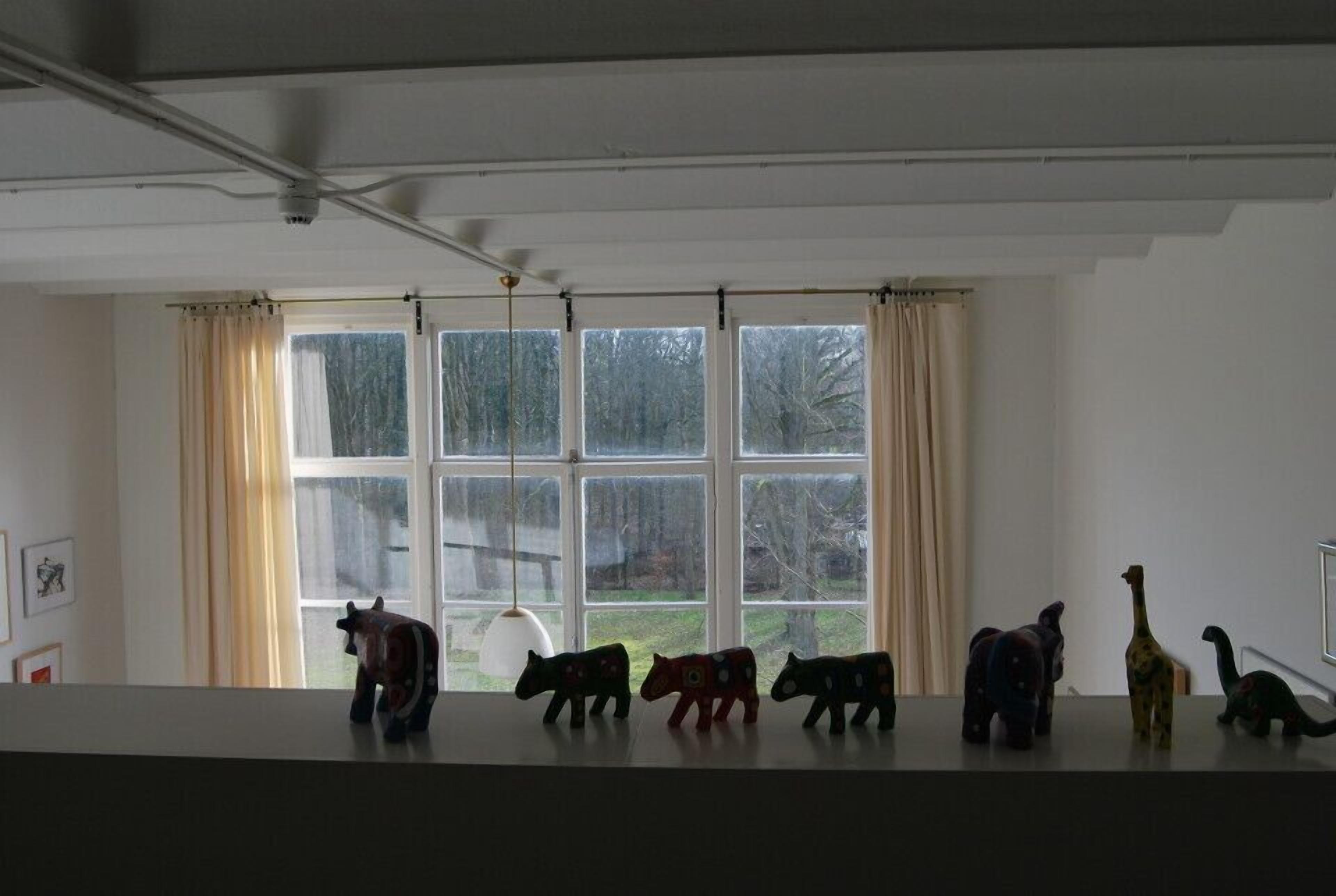 Quarto com uma janela grande, um ventilador de teto e uma estante com várias figurinhas de animais.