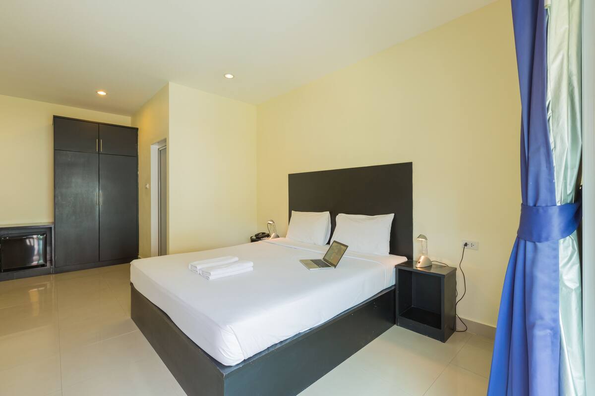 Quarto de hotel moderno com uma cama grande, mesas de cabeceira, escrivaninha e guarda-roupa.