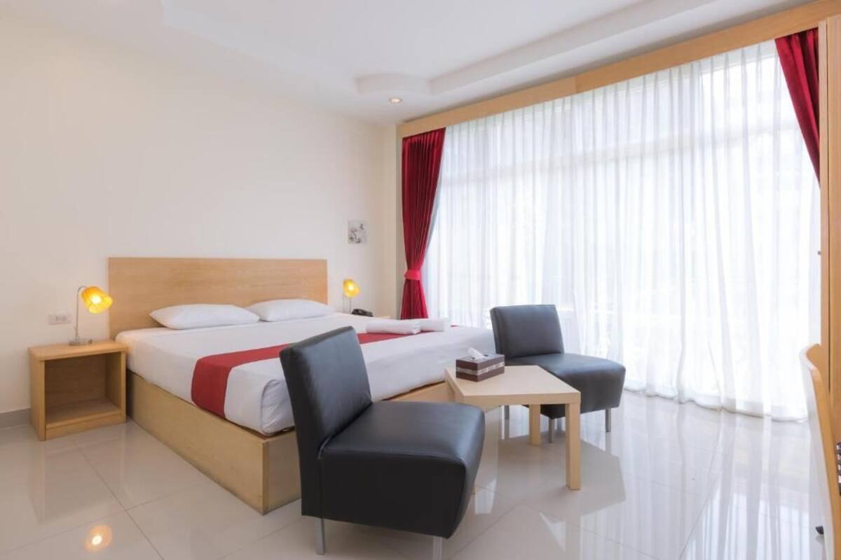 Quarto de hotel com cama, duas cadeiras, uma mesinha e um criado-mudo.