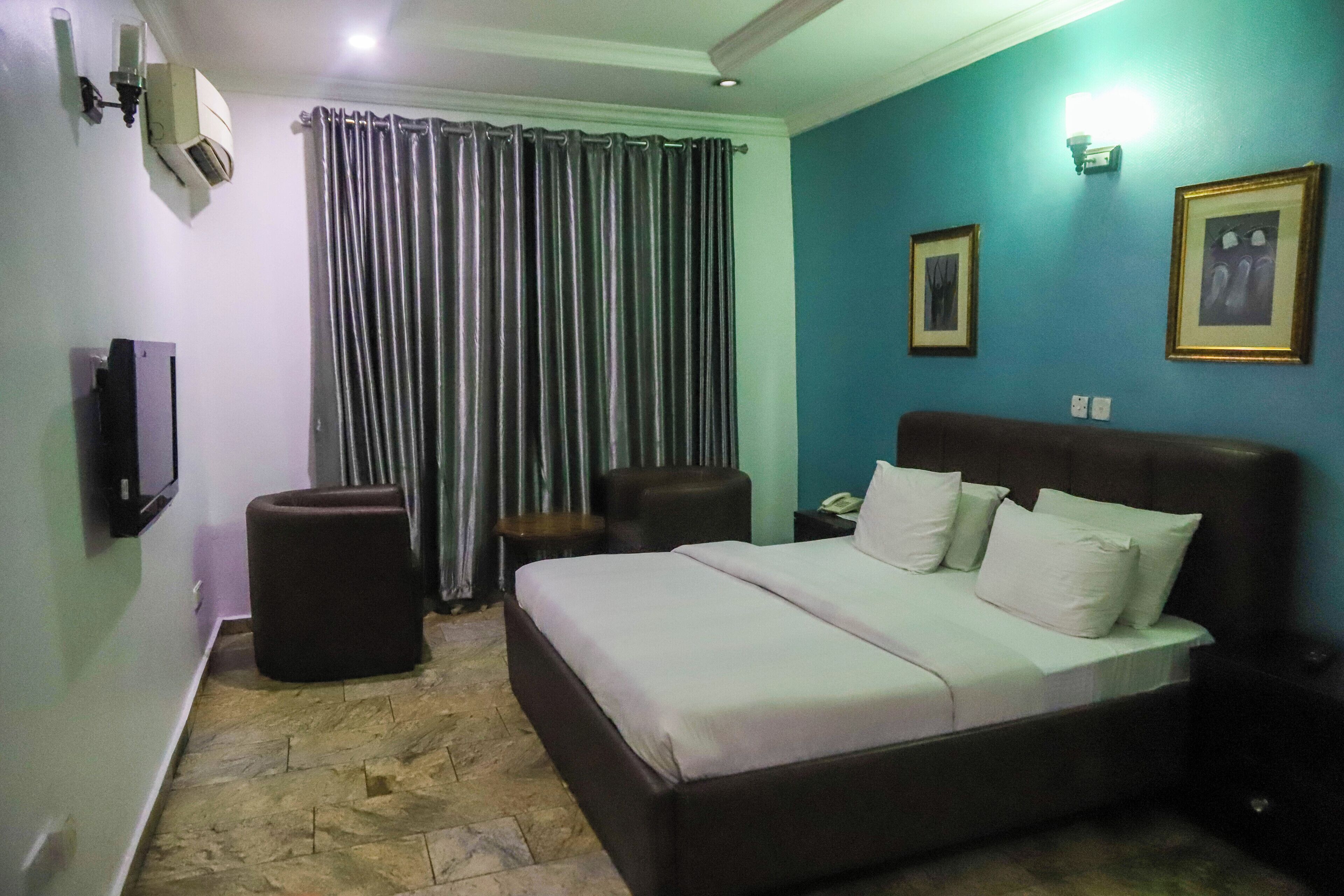 Quarto de hotel com cama, televisão, mesa pequena, cadeira e cortina.