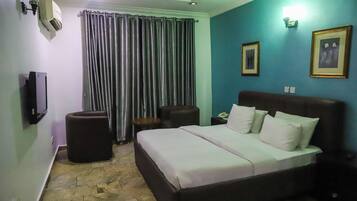 Quarto de hotel com cama, televisão, mesa pequena, cadeira e cortina.