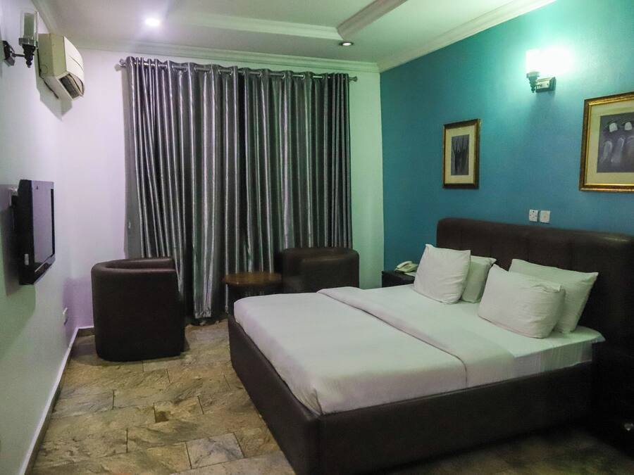 Quarto de hotel com cama, televisão, mesa pequena, cadeira e cortina.