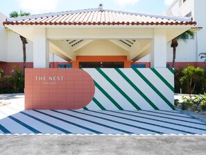 Entrada de um edifício com uma placa indicando 'THE NEST ISHIHAKI' e um caminho de azulejos que o leva até ele.