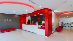 Uma área de recepção com esquema de cores vermelho e branco, um balcão com funcionários e áreas de estar.