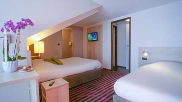 Quarto de hotel com uma cama, uma escrivaninha com luminária, uma televisão e uma orquídea em vaso.