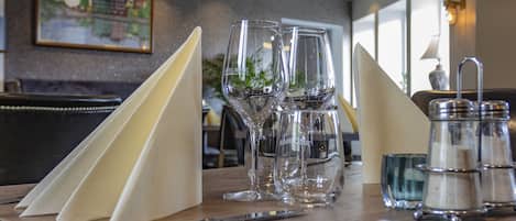 Uma mesa de jantar posta com taças de vinho, saleiro e pimenteiro, e um guardanapo dobrado.