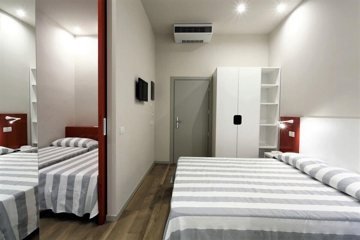 Quarto de hotel com duas camas, um guarda-roupa, uma TV e ar condicionado.