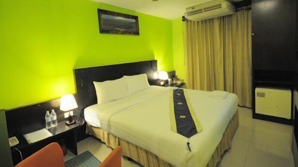 Quarto de hotel com cama, escrivaninha, cadeira, aparelho de ar condicionado e janela com cortinas.