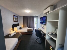 Quarto de hotel com duas camas, uma mesa com computador, uma cadeira, televisão e ar condicionado.