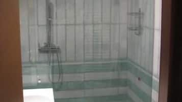 Casa de banho com cabine de chuveiro de vidro, sanita e lavatório.