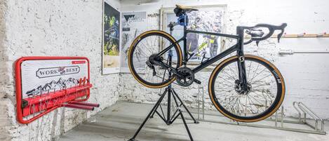 Uma bicicleta em um suporte em um quarto com parede de tijolos brancos, suporte de ferramentas vermelho e pôsteres.