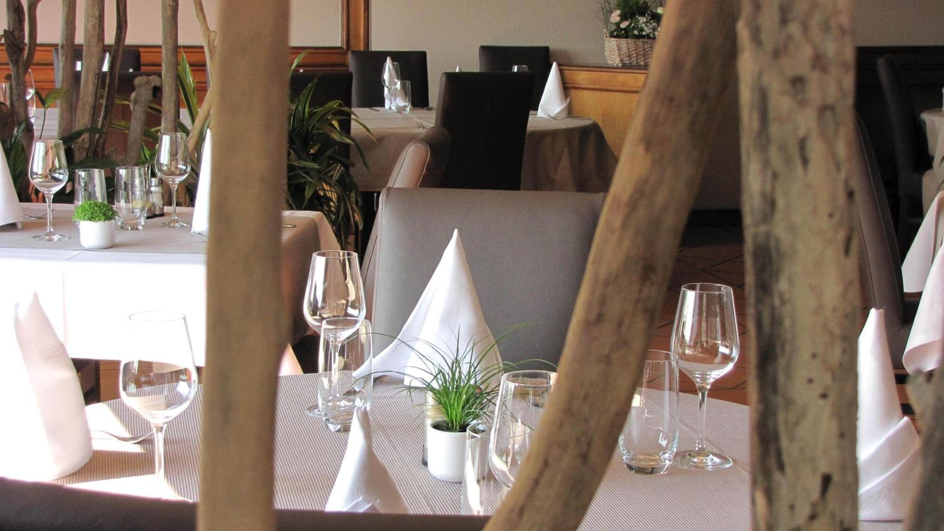 Ambiente de restaurante com mesas preparadas para refeições, com copos de vidro transparente e guardanapos brancos.