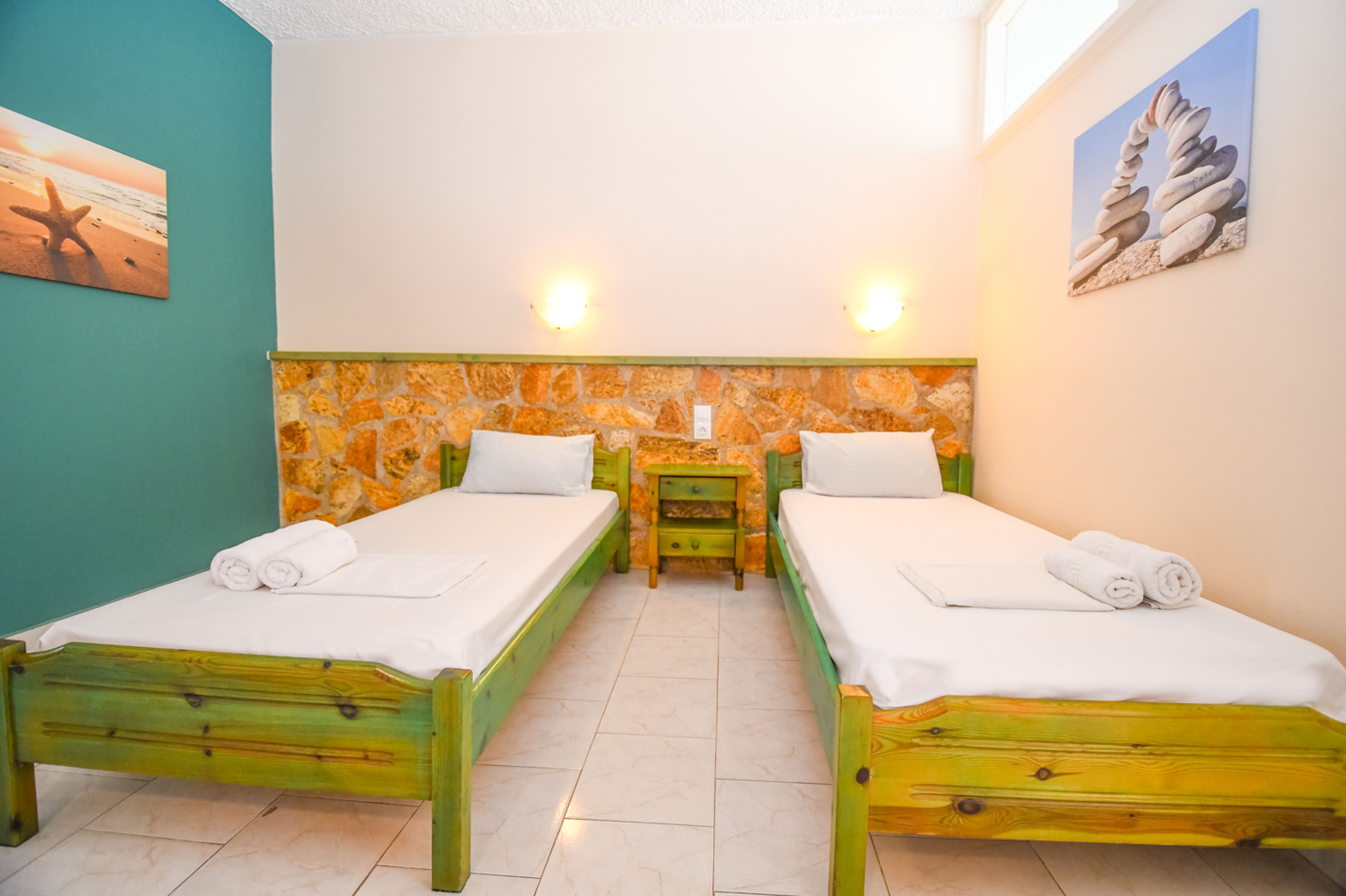 Quarto com duas camas de solteiro, uma mesinha e uma parede de pedra.