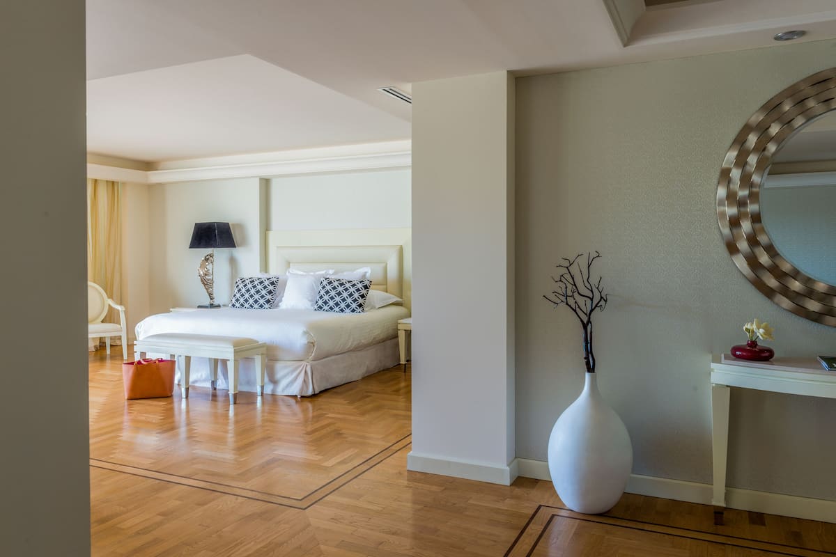 Quarto de hotel com cama, mesa de cabeceira, abajur e um vaso com galhos.