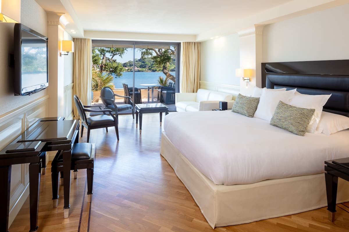 Quarto de hotel com uma cama grande, televisão, escrivaninha com cadeiras e varanda com vista para o mar.