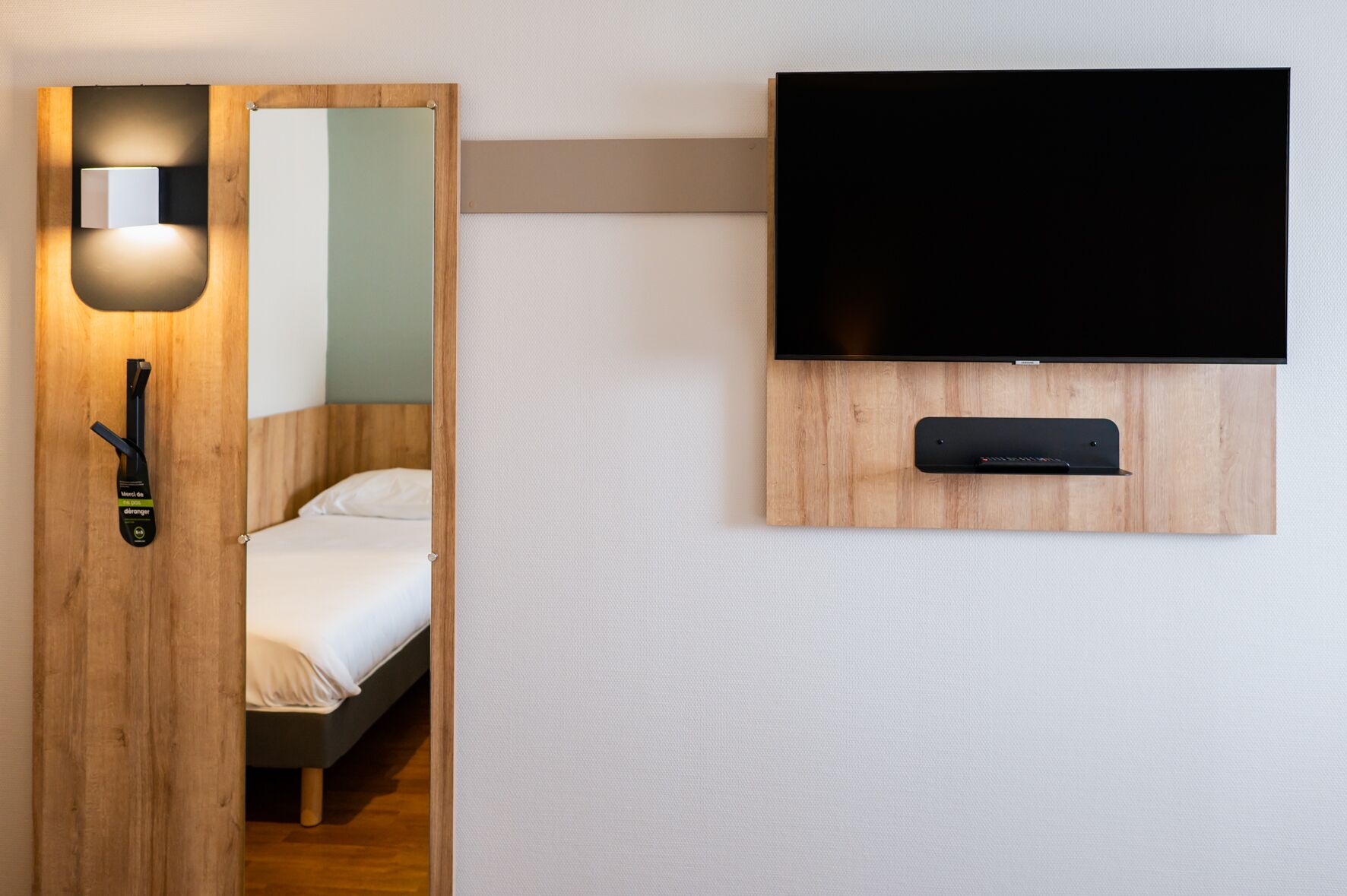 Quarto de hotel moderno com uma cama, uma porta de madeira, televisão na parede e painel de controle.