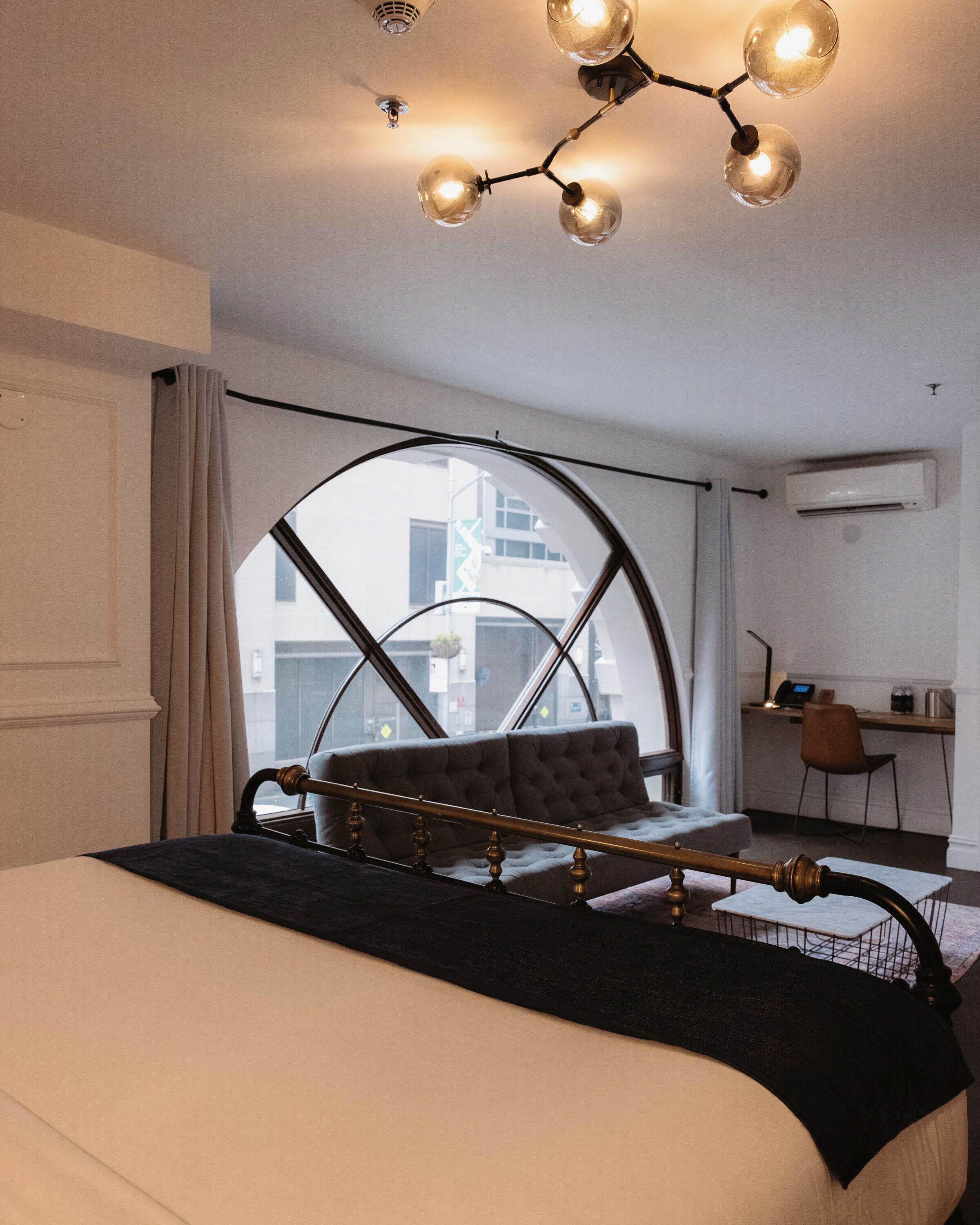 Quarto de hotel moderno com uma cama grande, um design de janela único, uma escrivaninha e um lustre moderno.