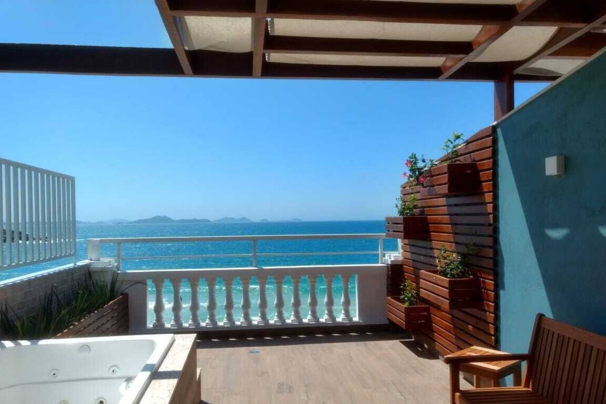 Uma varanda com vista para o mar, um banco de madeira e uma banheira branca.