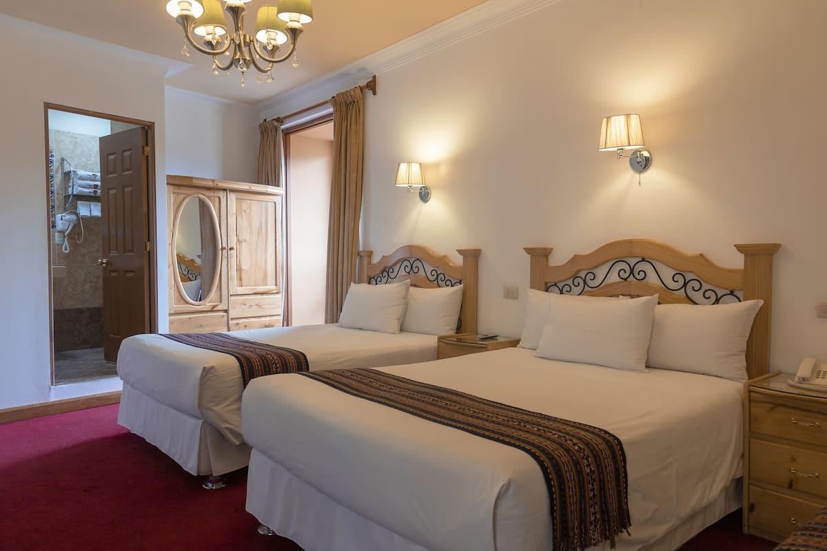 Quarto de hotel com duas camas, um guarda-roupa de madeira, um espelho e um candelabro.