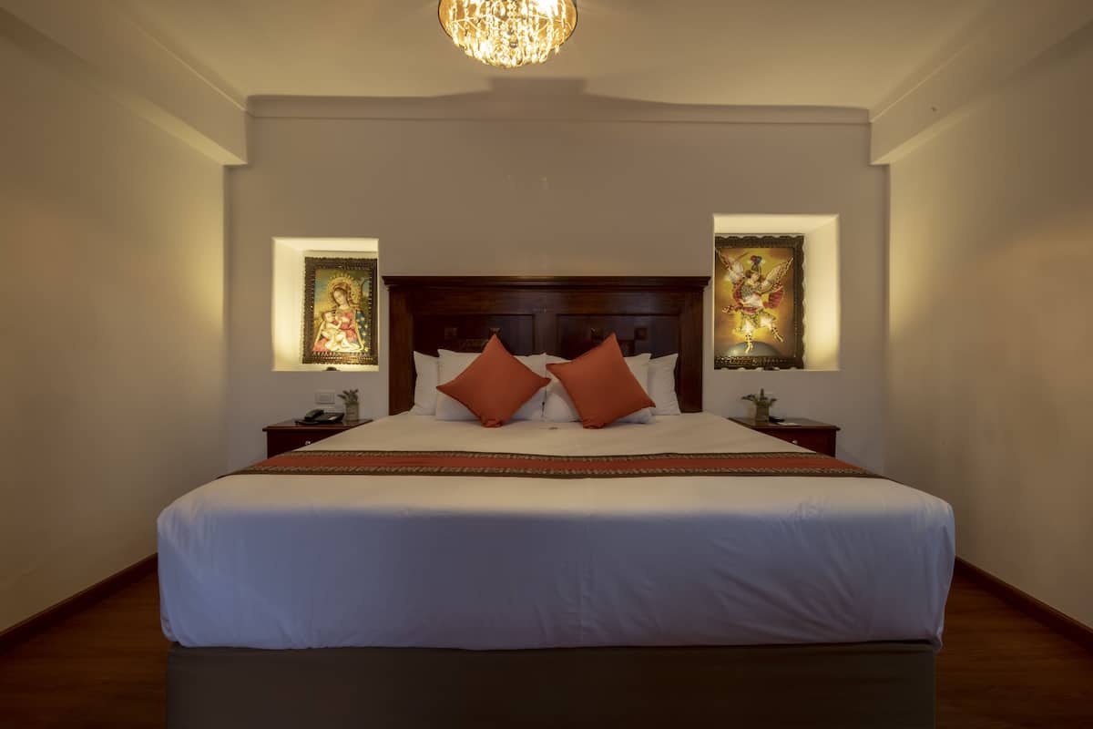 Uma cama grande com lençóis brancos e duas almofadas laranja, com duas mesas de cabeceira com obras de arte emolduradas de cada lado.