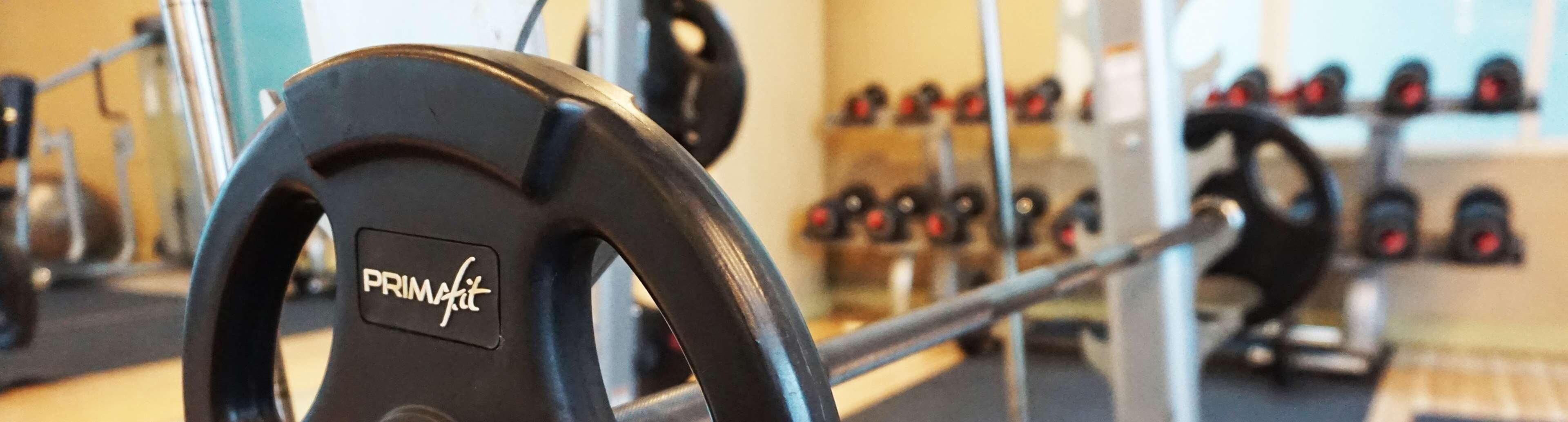 Uma academia com equipamento de musculação, incluindo barra e halteres.