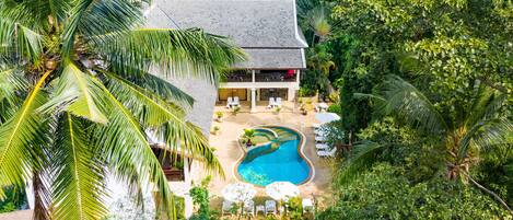 Uma casa de dois andares com piscina, rodeada por vegetação exuberante.