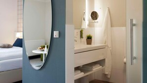 Quarto moderno com um espelho oval grande, uma cama, mesa de cabeceira com abajur e banheiro com vaso sanitário, pia e porta-toalhas.