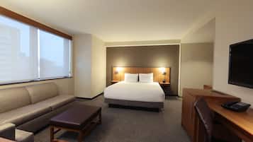 Quarto de hotel com cama, sofá, escrivaninha e televisão.