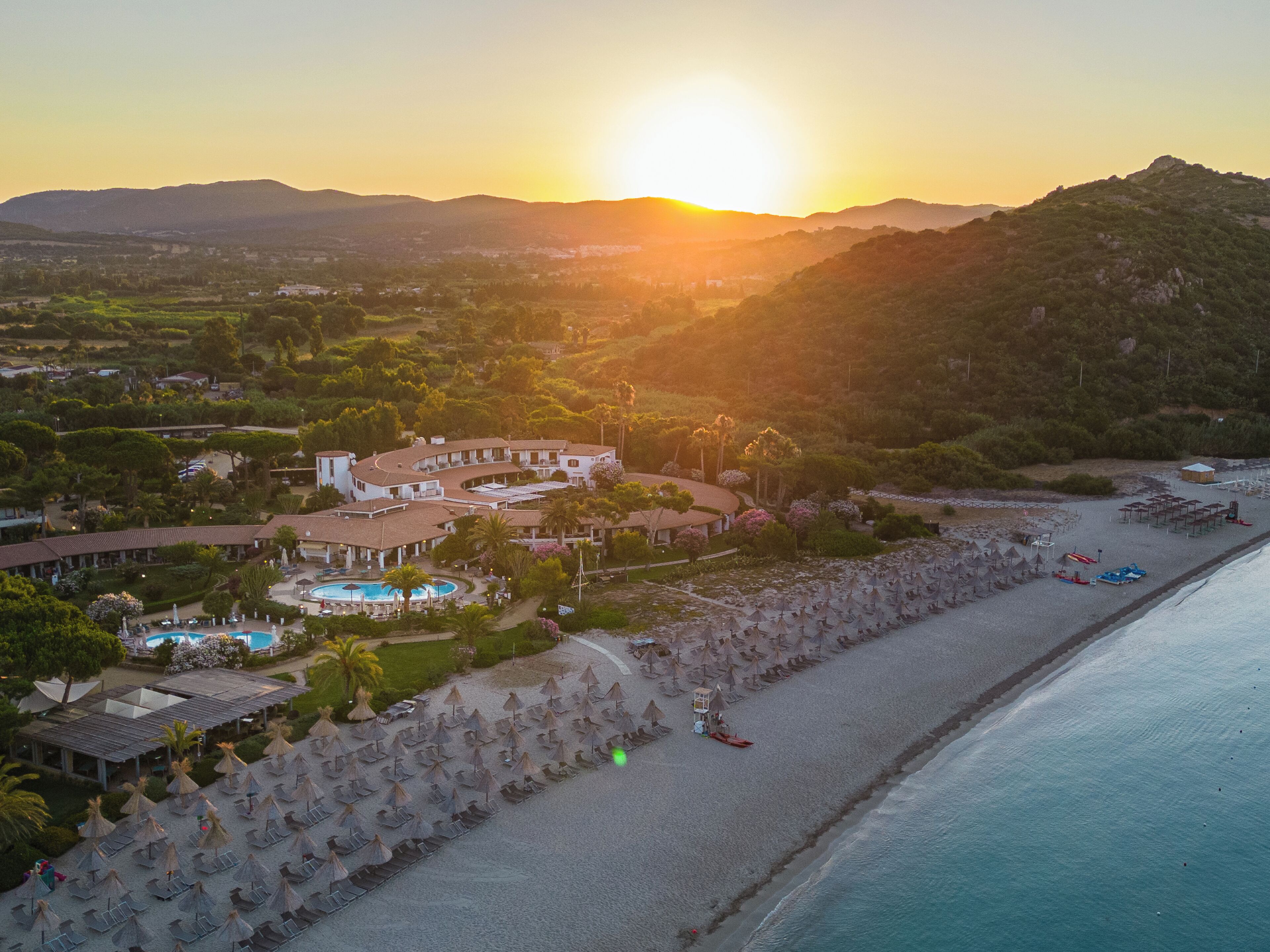 Um resort com piscina, guarda-sóis e vista para o pôr do sol sobre as colinas.