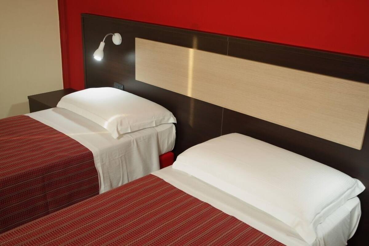 Quarto de hotel com duas camas, cada uma com colcha listrada de vermelho e branco.
