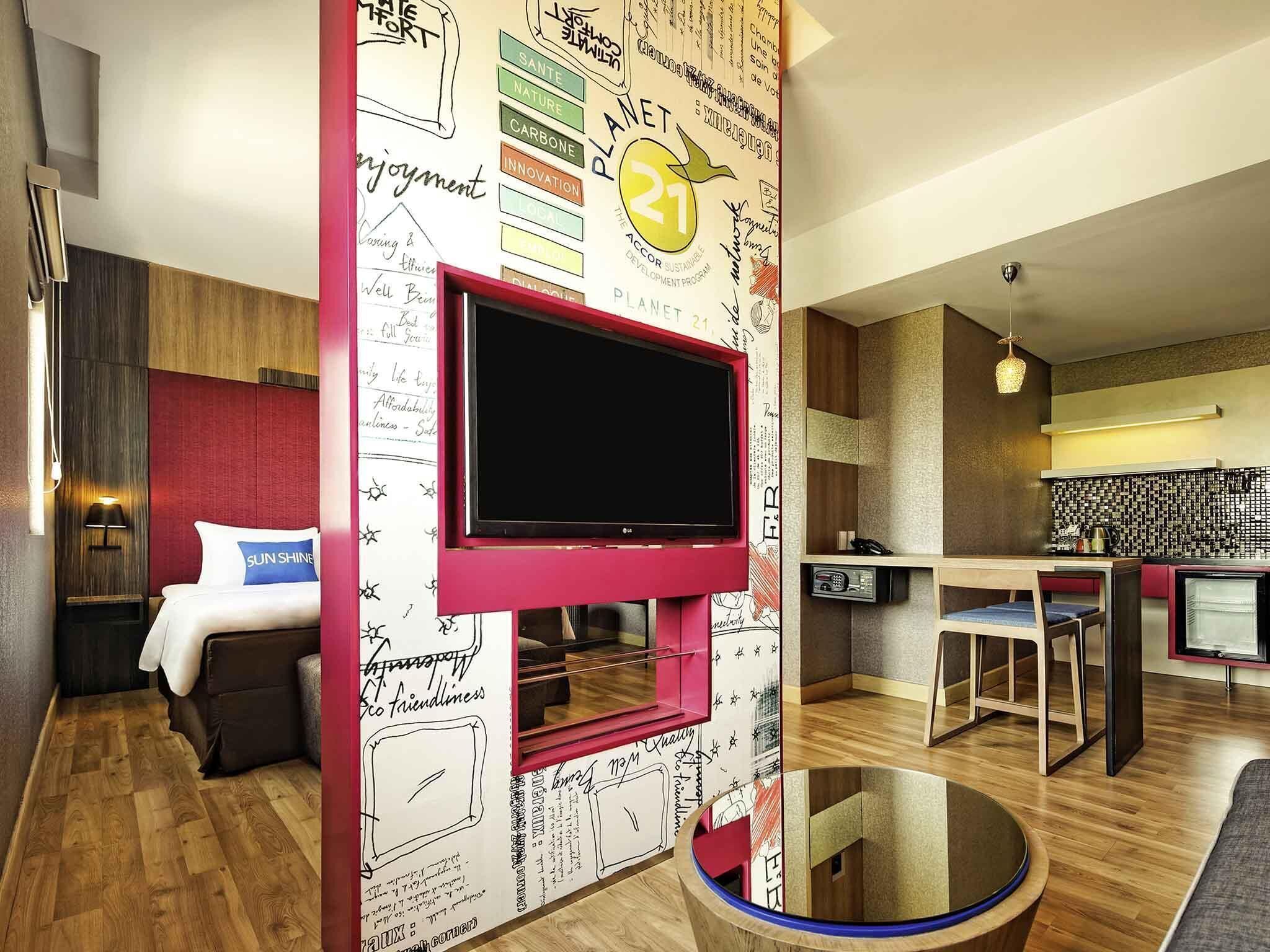Quarto de hotel moderno com uma televisão de tela grande, um pequeno espaço para refeições e um local de estar acolhedor.