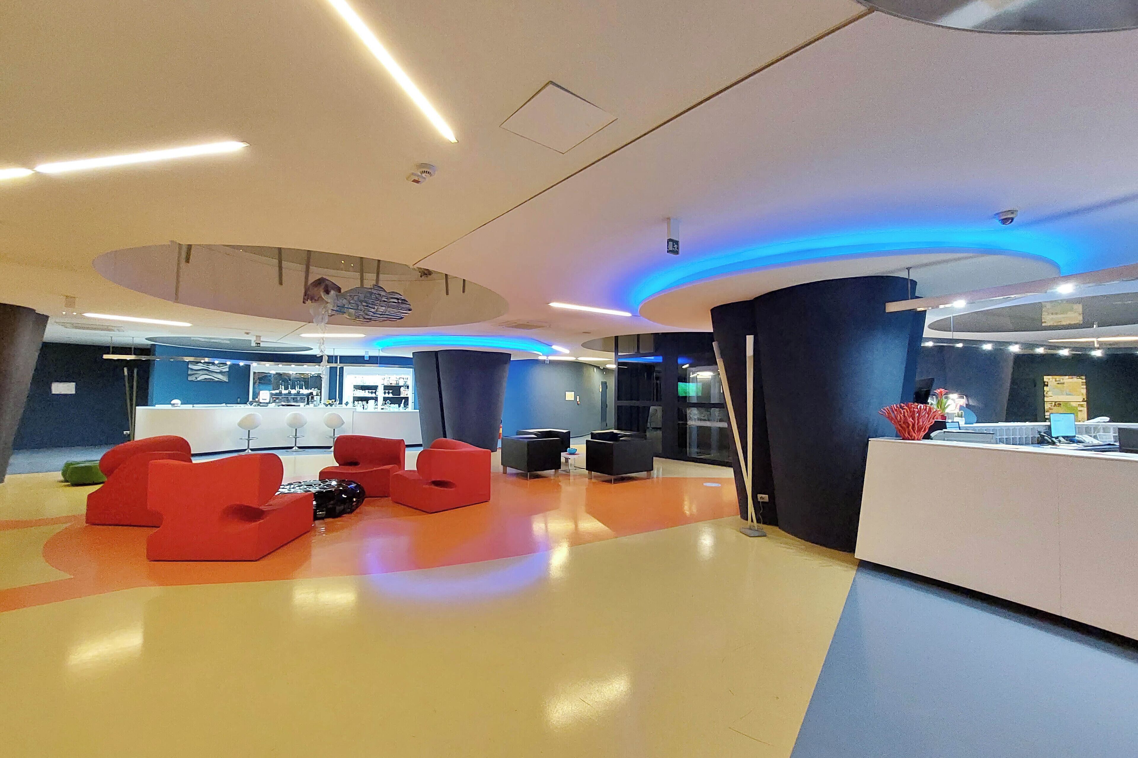 Um hall moderno com balcão de recepção, área de estar e teto iluminado em azul.