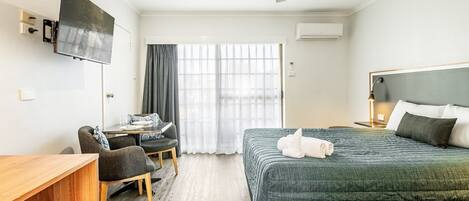 Quarto de hotel com cama, escrivaninha, cadeira, televisão e ventoinha no teto.