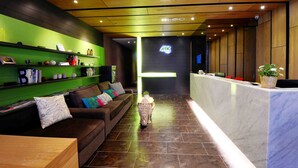 Uma área de recepção com parede verde, balcão de madeira e sofá marrom com almofadas decorativas.