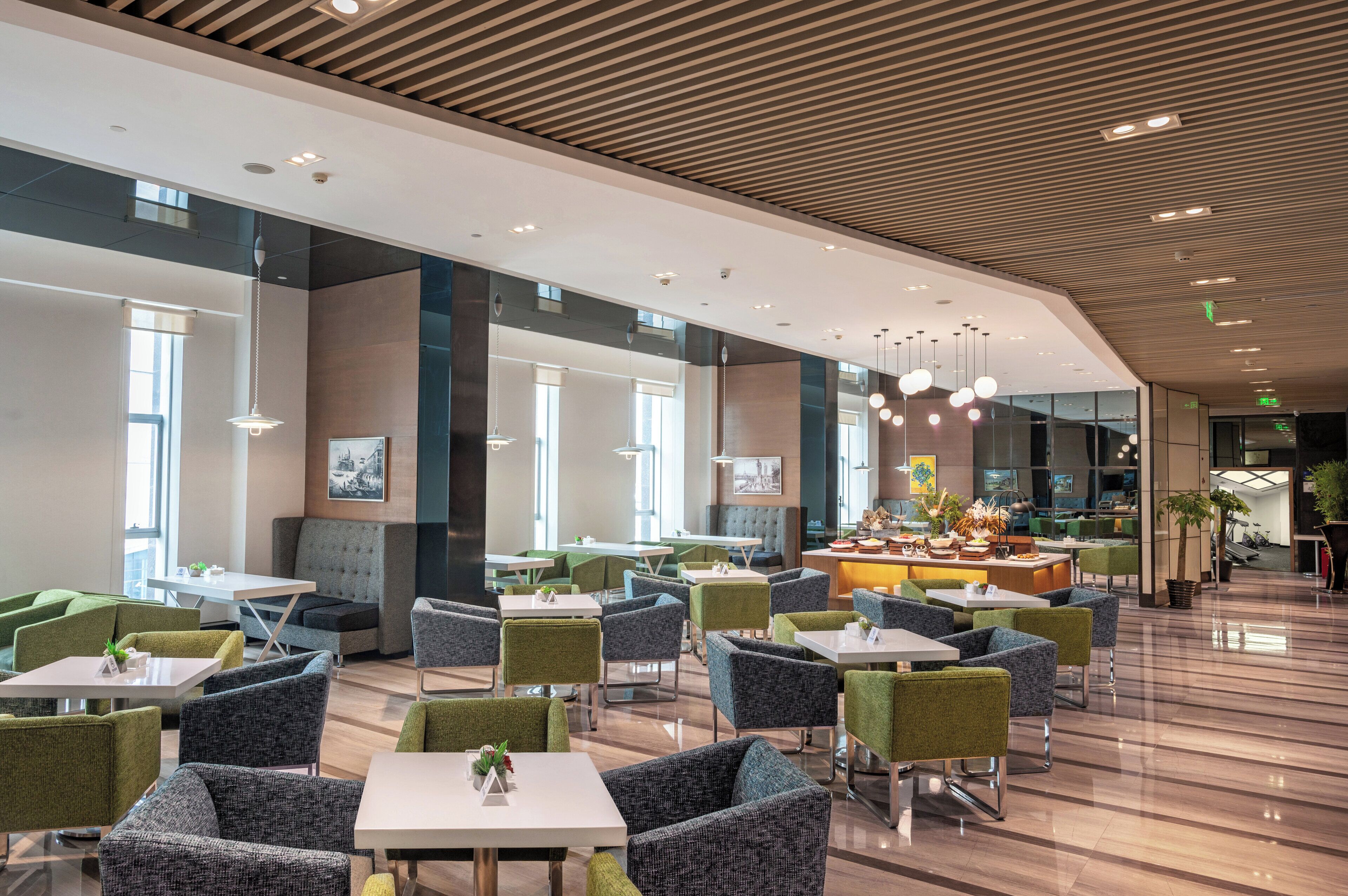 Um hall de hotel moderno com áreas de estar, mesas e um bar central.