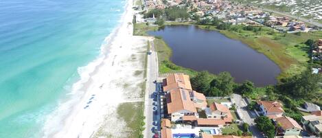 Vista aérea de uma área costeira com uma praia, um pequeno lago e edifícios residenciais.
