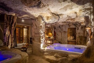 Uma área de spa com banheira de hidromassagem, mobiliário de madeira e decoração rústica que lembra uma caverna.