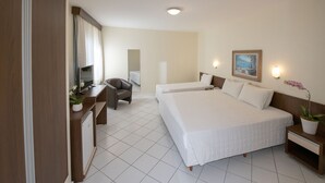 Quarto de hotel com duas camas, uma escrivaninha, uma cadeira, televisão e um vaso de plantas.
