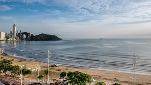 Paisagem costeira com praia, um arranha-céu imponente e uma ilha montanhosa ao longe.